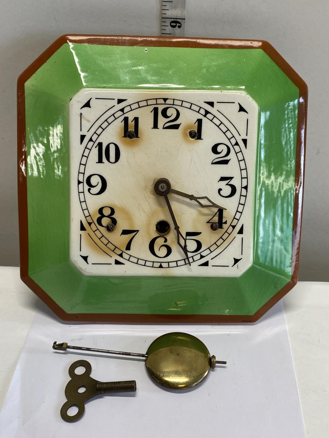 A unusual antique ceramic faced wall clock with pendulum and key