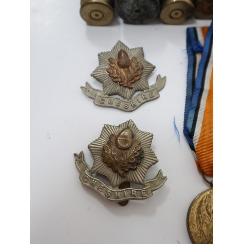 A collection of spent ammunition shells, two Cheshire Regiment Cap ...