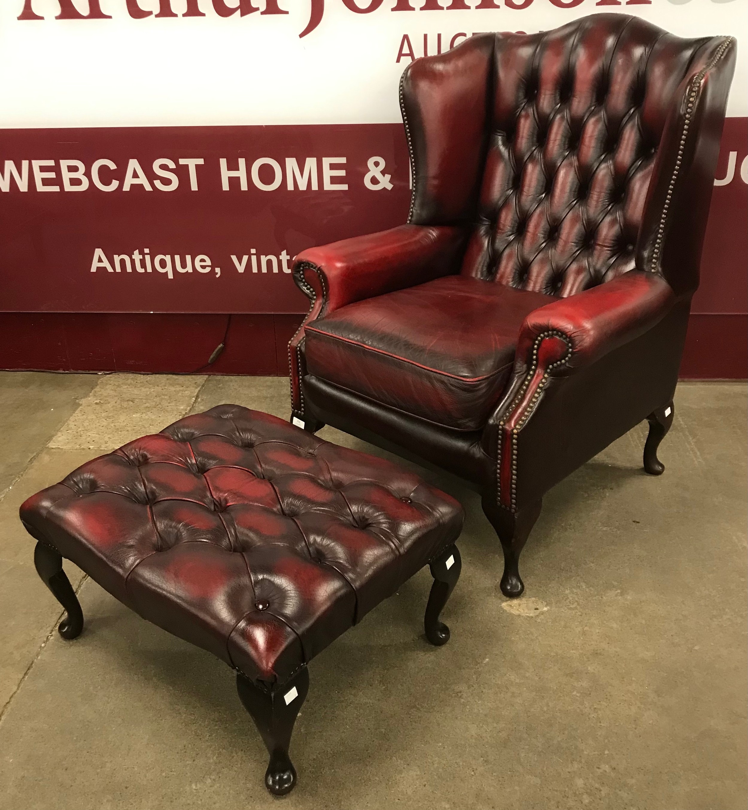 An oxblood red leather Chesterfield wingback armchair and footstool