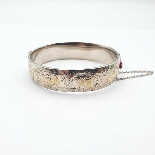 A hinged Silver Bangle engraved with thistles with gold detailing ...