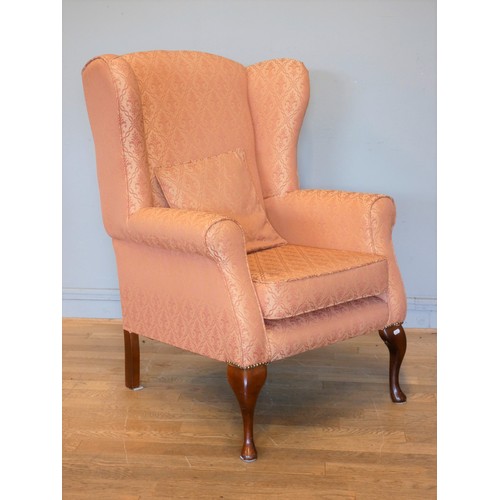 A modern wingback armchair, upholstered in a a fleur de lys pink ...