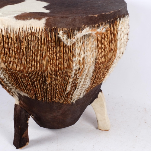 An African cow skin drum resting on 3 feet, with 2 carrying handles ...