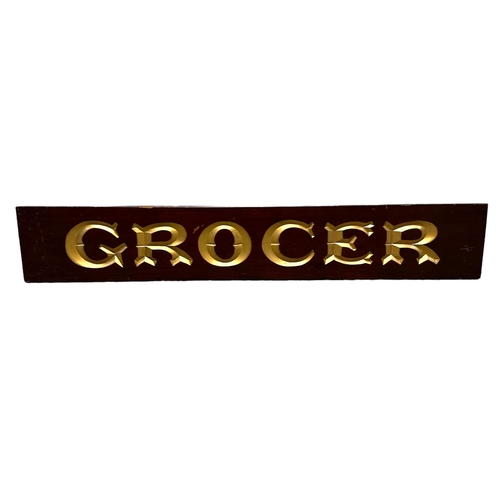 A decorative sign 'GROCER' with carved gilt lettering, 122 by 20cms.