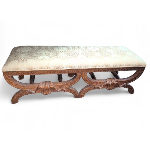 Heavily-carved upholstered long footstool. W137cm D44cm H46cm.