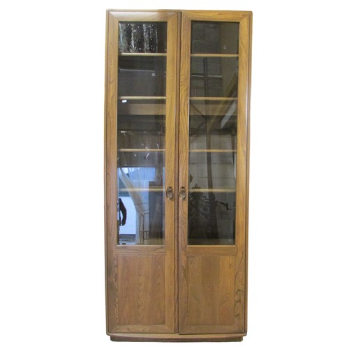 A Ercol elm upright bookcase, enclosed by a pair of full length doors ...