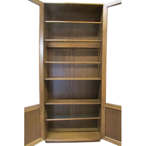 A Ercol elm upright bookcase, enclosed by a pair of full length doors ...