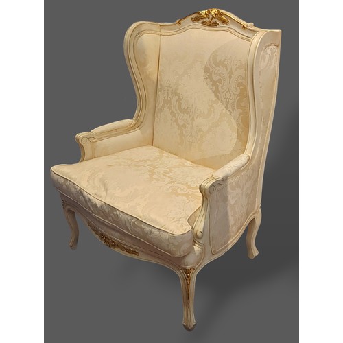 A French cream painted wingback armchair with carved gilded decoration ...