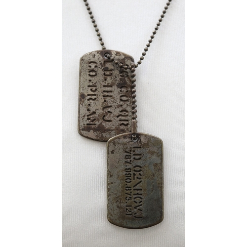 A pair of military-style metal identity tags, each suspended on a ball ...
