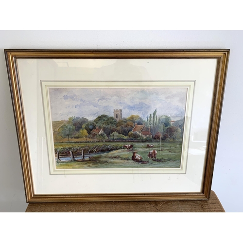 A framed and glazed watercolour of cows in a field with a church in the ...