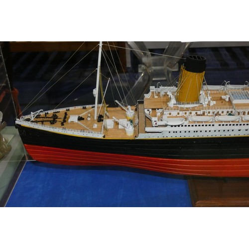 A perspex display cabinet containing a wooden model of RMS Titanic