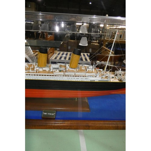 A perspex display cabinet containing a wooden model of RMS Titanic