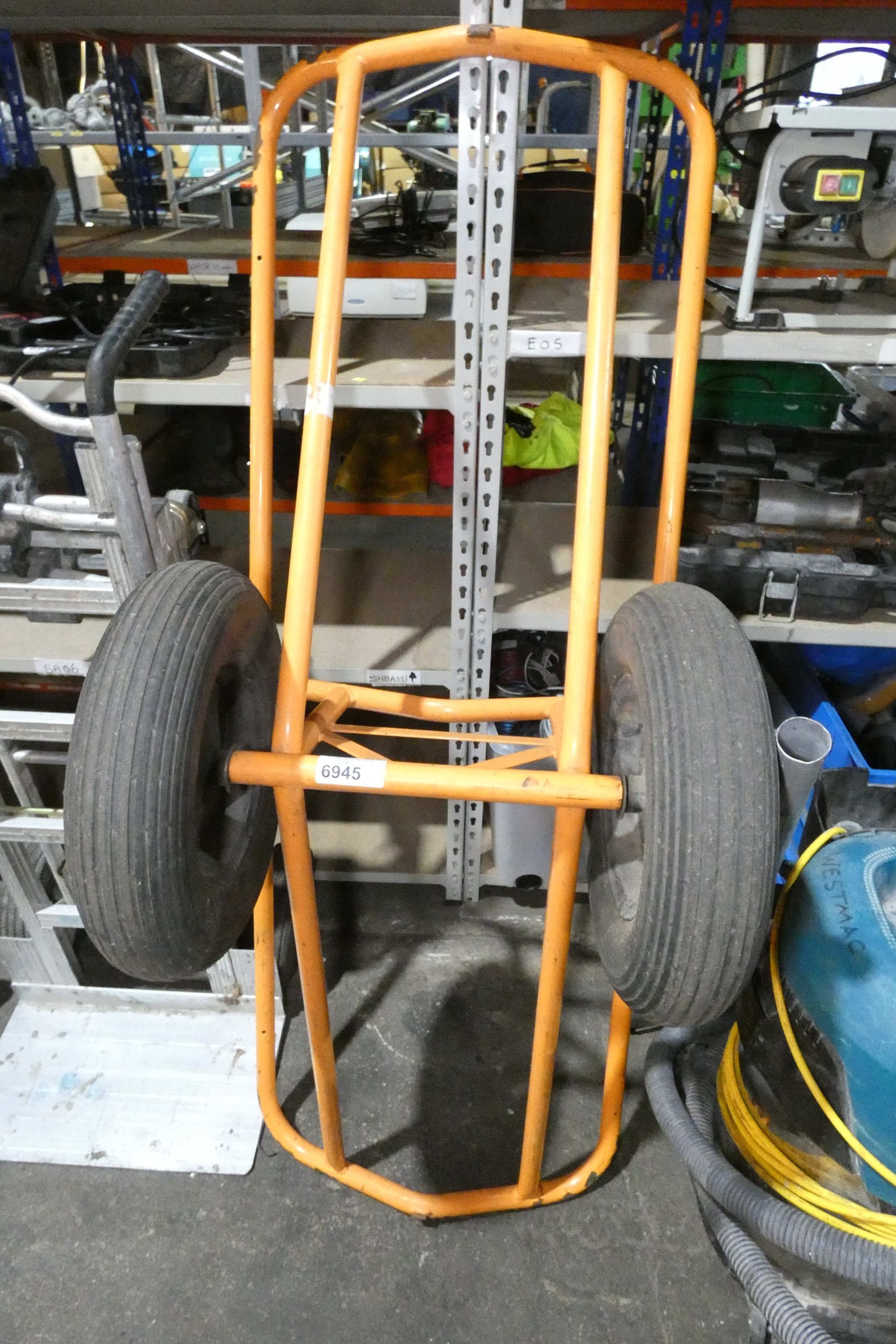 An orange metal two wheeled trolley for moving rolls of floor covering ...