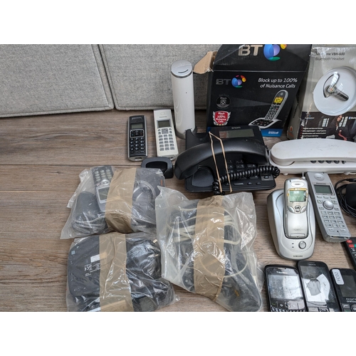 A collection of landline telephones, remote controls and mobile phones ...