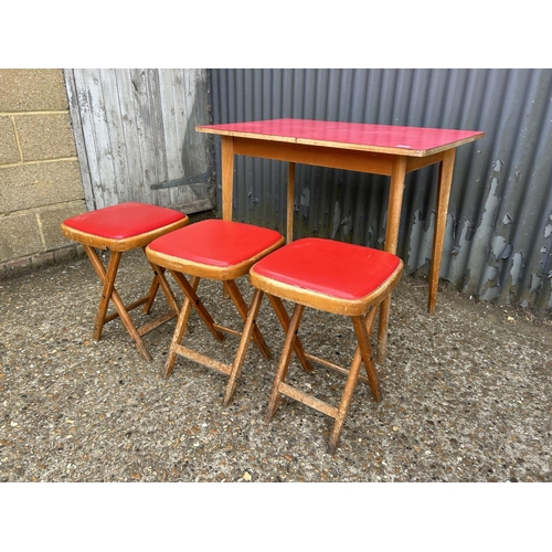 A red formica kitchen table and three folding stools