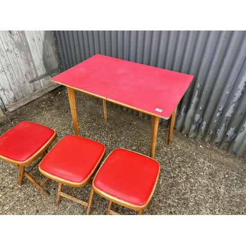A red formica kitchen table and three folding stools