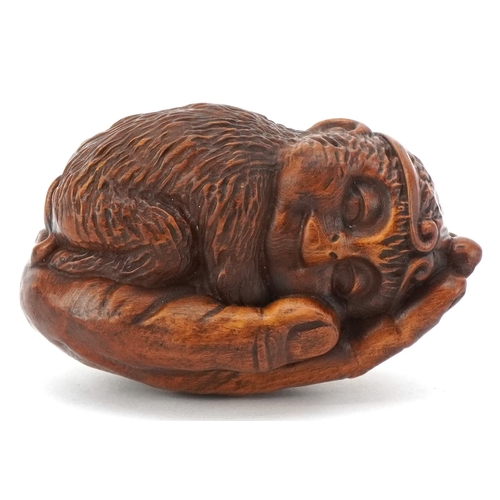 A Japanese carved boxwood okimono in the form of a monkey in the palm ...