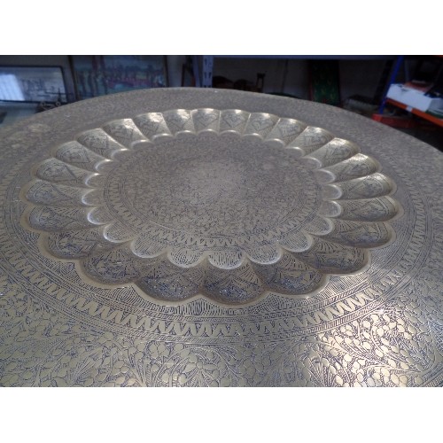 AN EARLY 20TH CENTURY BENARES BRASS TABLE ON ORNATELY CARVED FOLDING ...